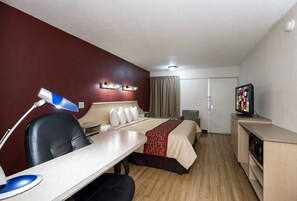 Quarto de hotel com escrivaninha, cadeira, cama, televisão e porta do banheiro.