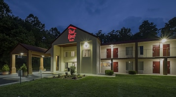 Um motel com letreiro de neon, área de estacionamento coberta e gramado bem cuidado.