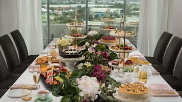 Mesa posta para um evento formal, com vários níveis de comida, arranjos florais e bebidas.