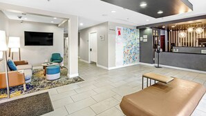 Um lobby moderno com uma mesa de recepção, área de estar e uma televisão de tela plana na parede.
