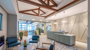 Um lobby moderno com balcão de recepção, área de estar com mesas e cadeiras, e piso estampado.