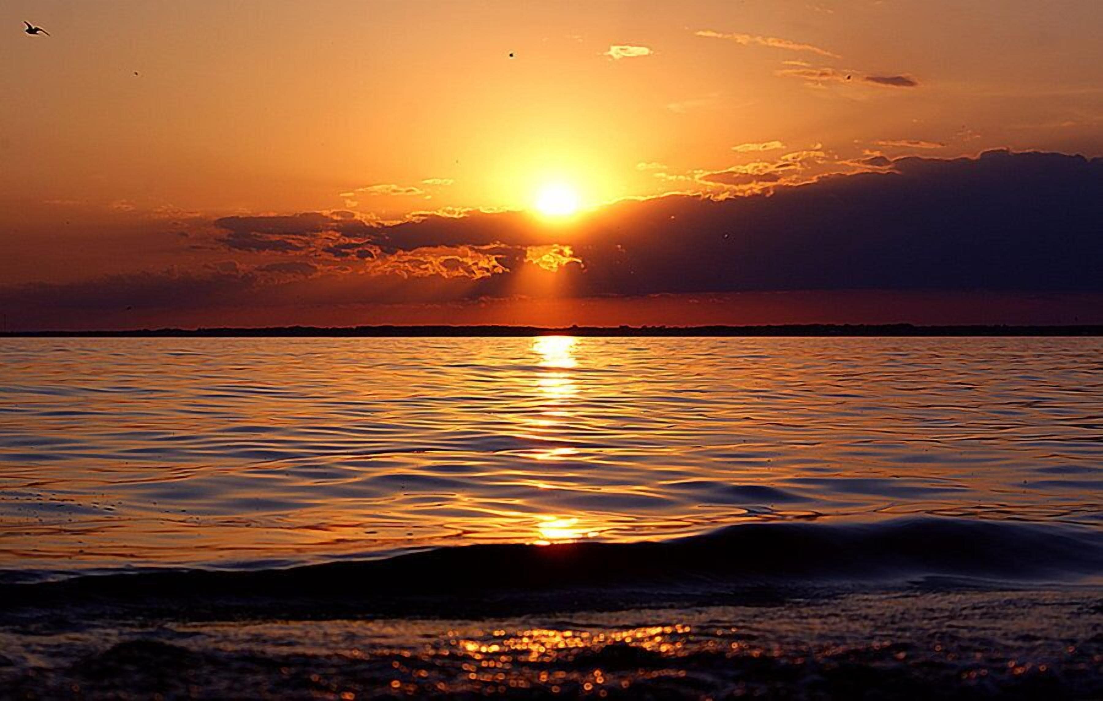 Um pôr do sol sobre um mar calmo, com horizonte nítido.