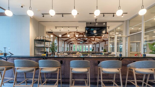 Uma área de bar moderna com teto alto, iluminação pendente e um balcão central com banquetas.