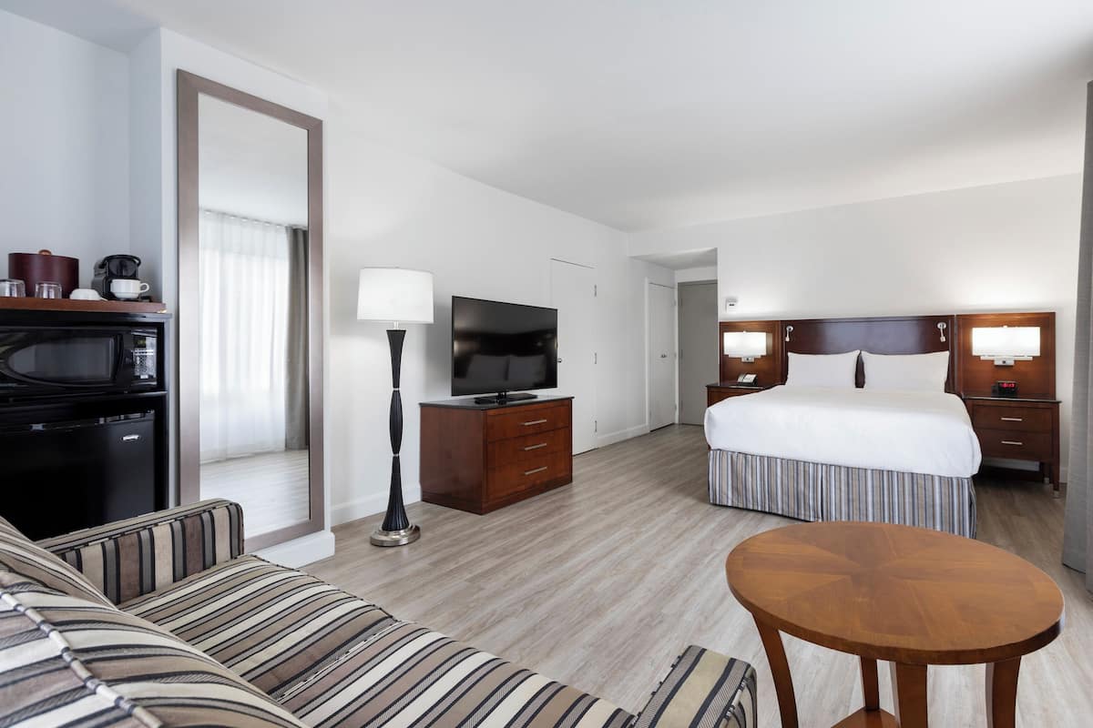 Quarto de hotel com cama, televisão, máquina de café, micro-ondas, sofá e uma pequena mesa.