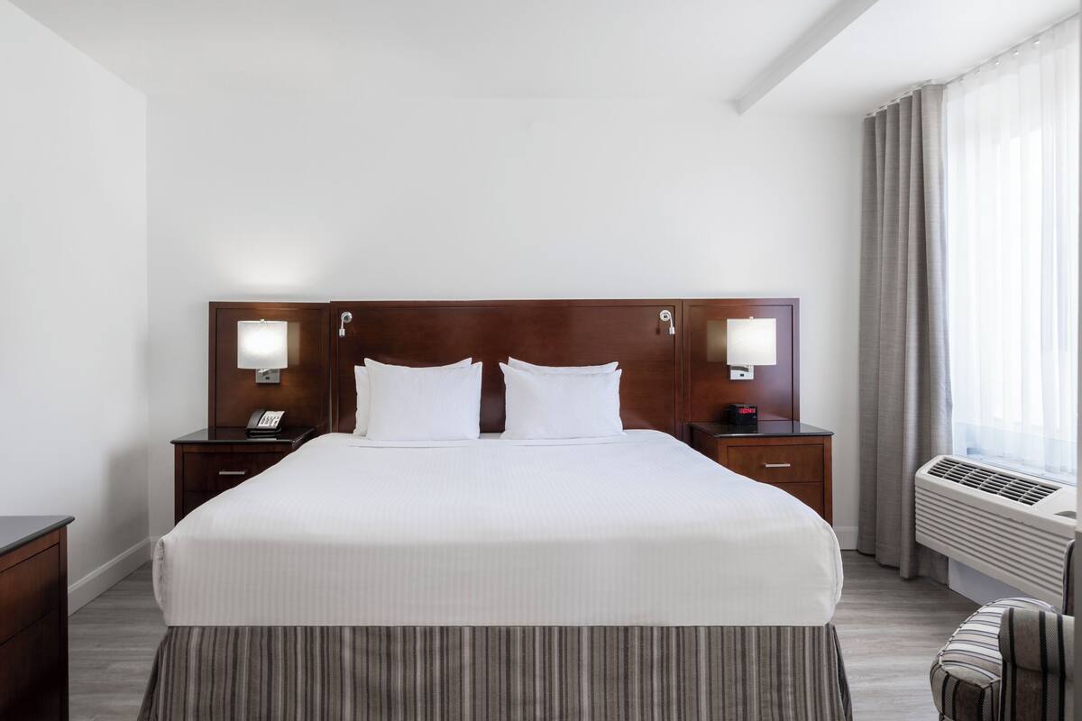 Quarto de hotel com uma cama grande, duas mesas de cabeceira com abajures, uma televisão de tela plana e uma janela com cortinas.