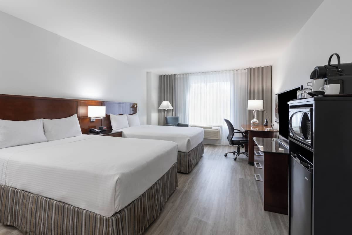 Quarto de hotel com duas camas, uma escrivaninha com computador, televisão, micro-ondas e minibar.