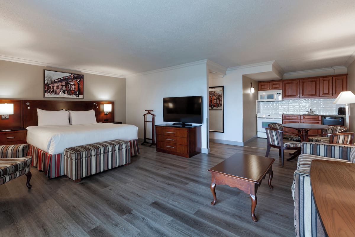 Quarto de hotel com cama, televisão, mesa de jantar e cozinha.