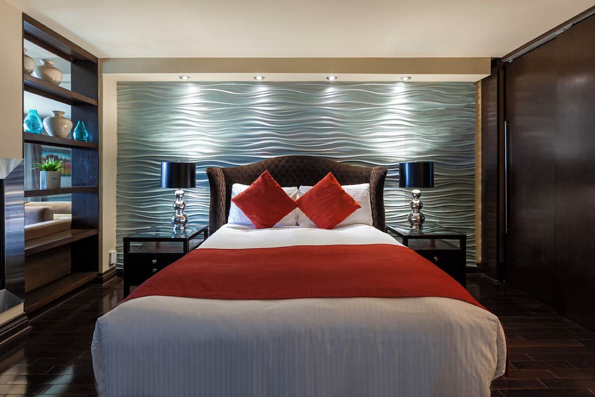 Quarto de hotel moderno com uma cama grande, duas mesas de cabeceira, um painel de madeira e um detalhe decorativo na parede.