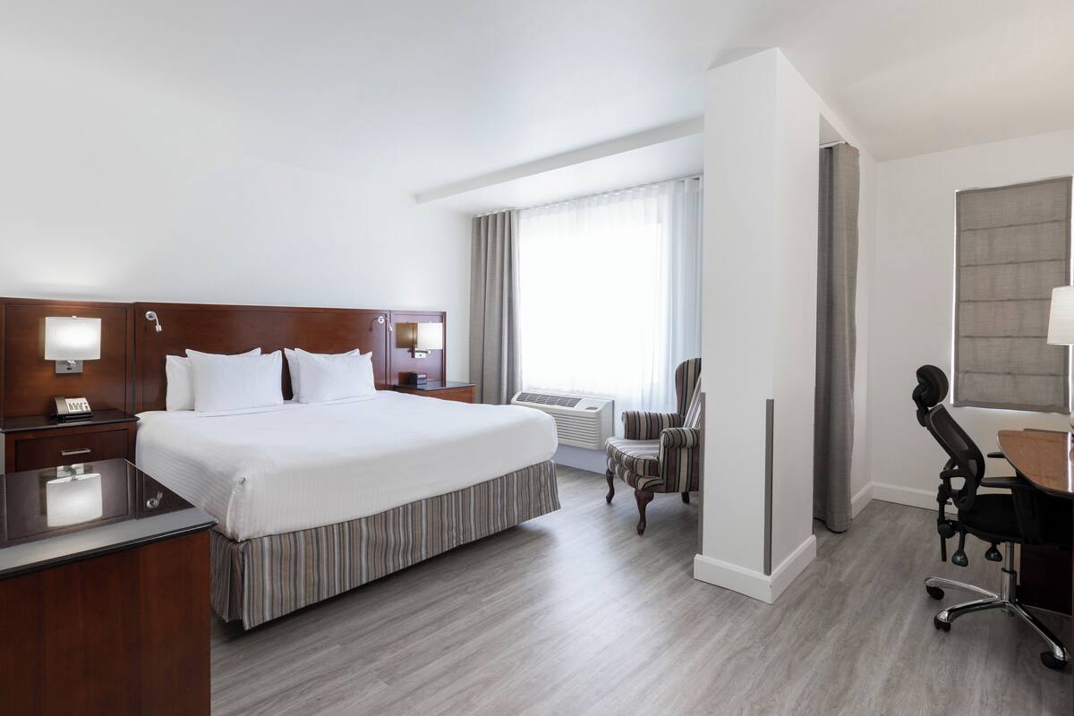 Quarto de hotel com cama grande, mesas de cabeceira, escrivaninha e cadeira, e janela com cortinas.