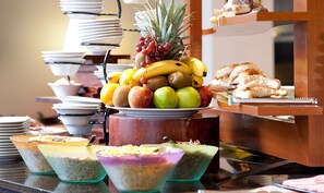 Buffet com variedade de frutas, incluindo bananas, maçãs e kiwis, e várias tigelas de cereais.