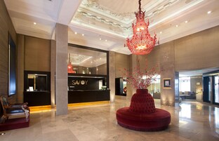 Um lobby com balcão de recepção, área de estar estofada em vermelho e um candelabro.