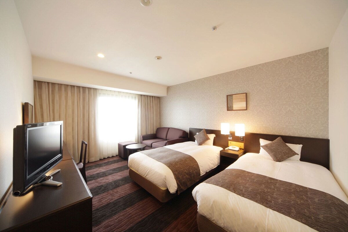 Quarto de hotel com duas camas, televisão, escrivaninha e uma cadeira.