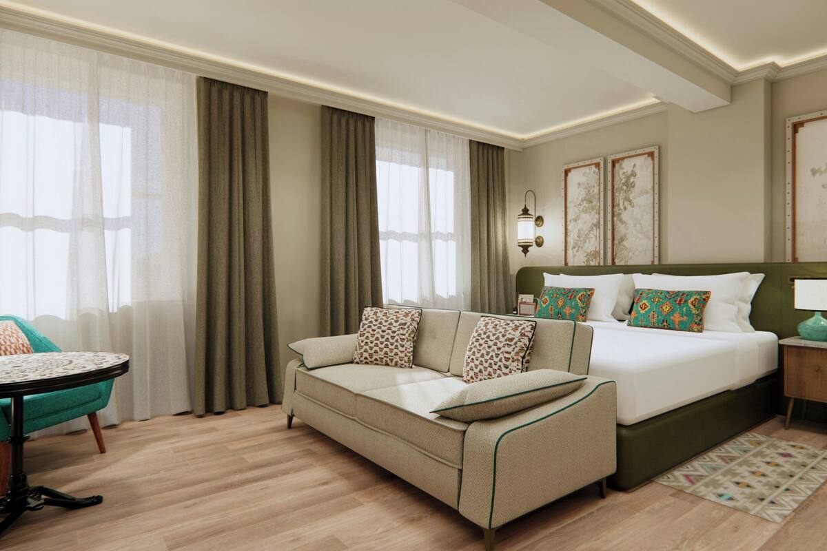 Quarto de hotel com cama, sofá, uma mesinha e janela com cortinas.