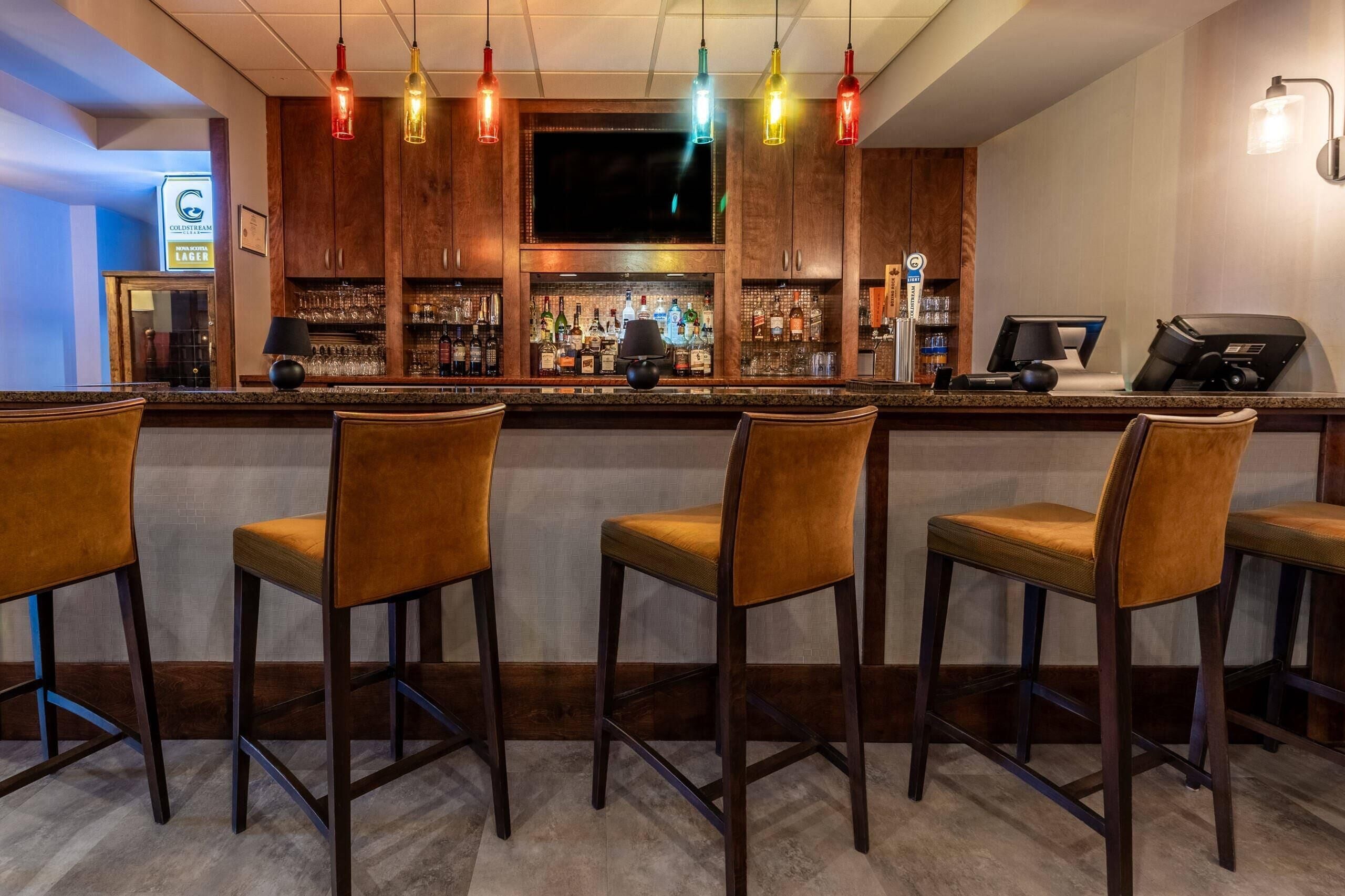 Uma área de bar com balcões de madeira, vários bancos, uma televisão acima do balcão e um letreiro de Coors Light Lager.