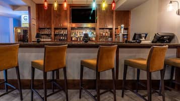 Uma área de bar com balcões de madeira, vários bancos, uma televisão acima do balcão e um letreiro de Coors Light Lager.