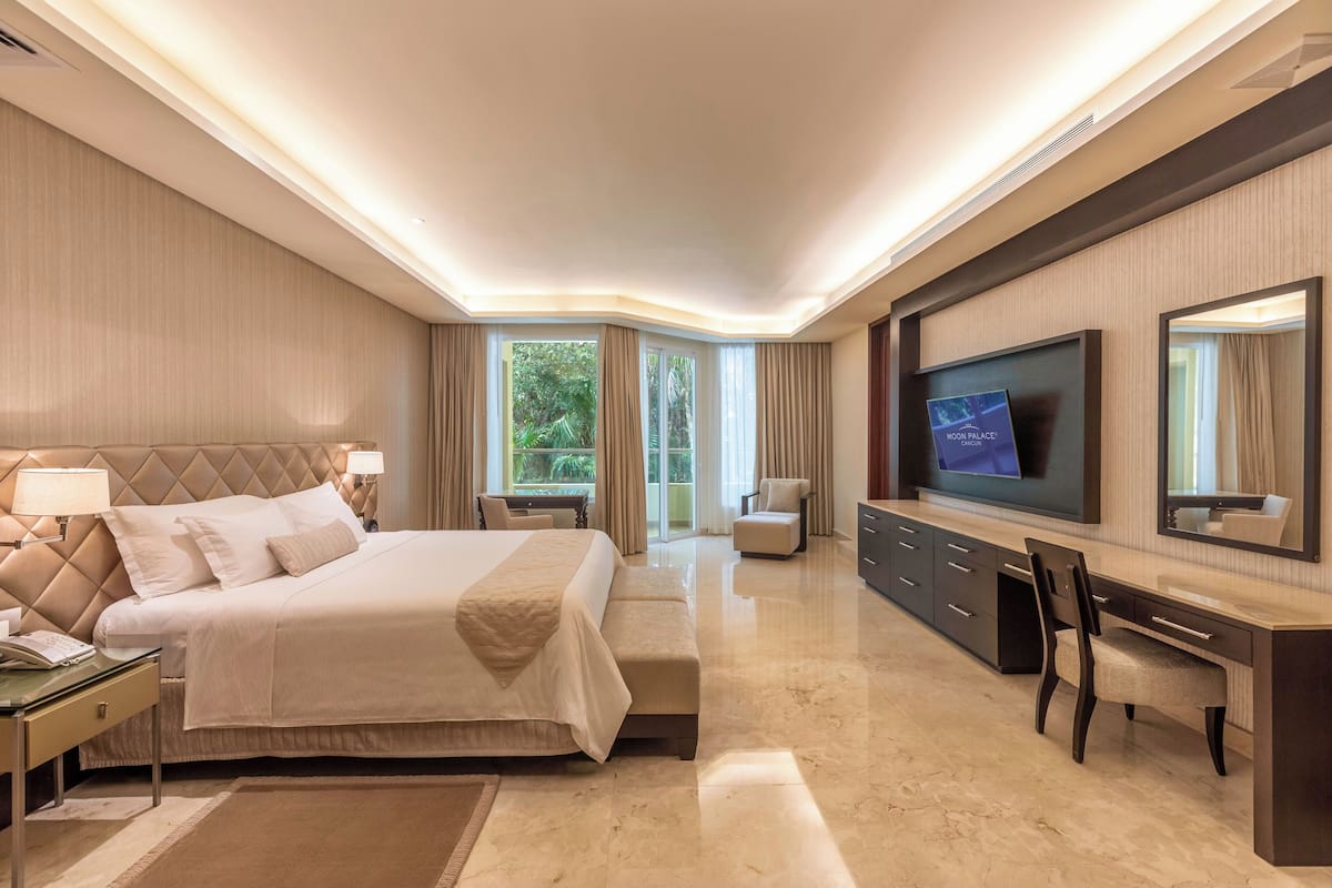 Quarto de hotel moderno com uma cama grande, uma escrivaninha, televisão e vista para o verde lá fora.