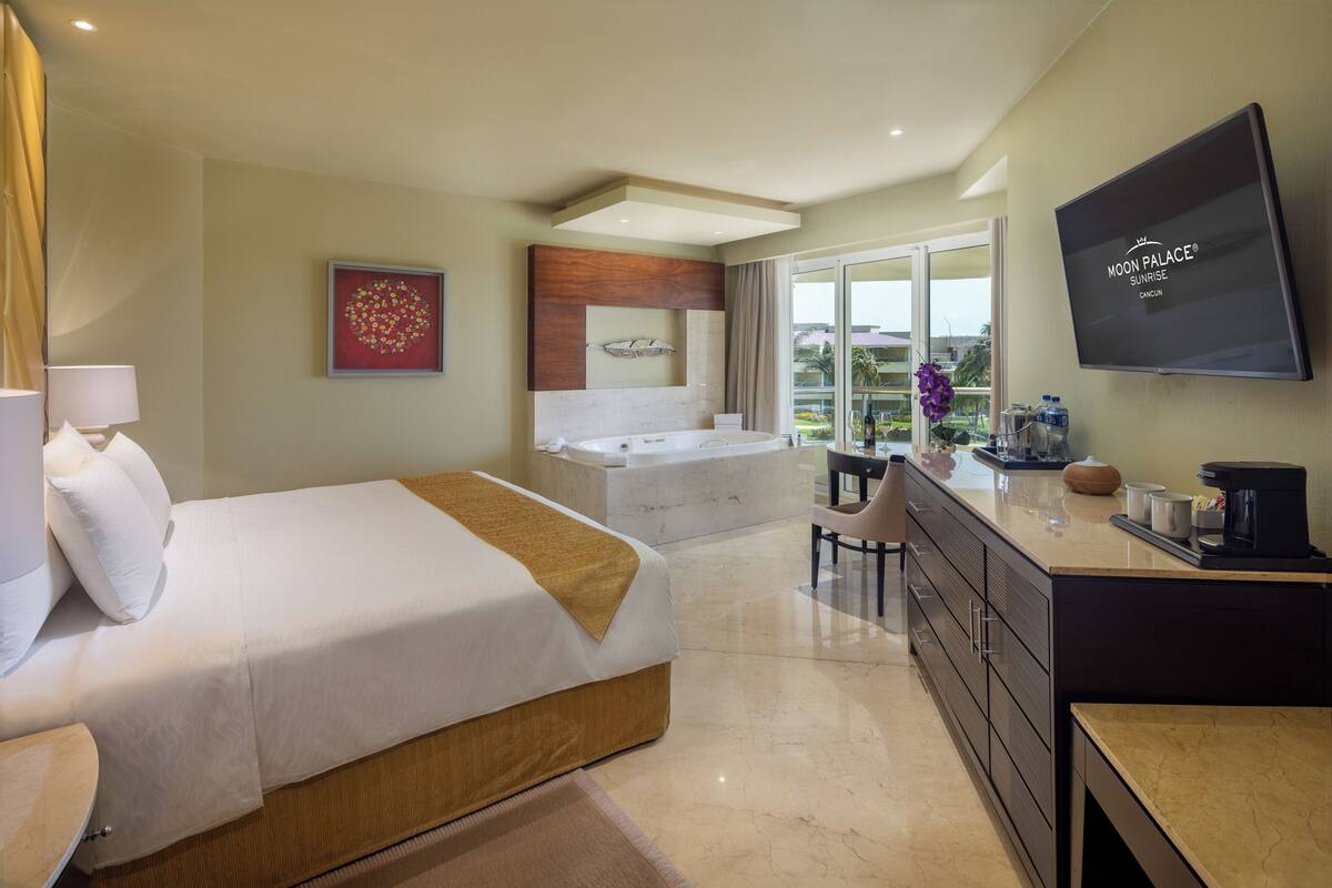 Quarto de hotel com cama, escrivaninha, cadeira, televisão, banheira e vista para o exterior.