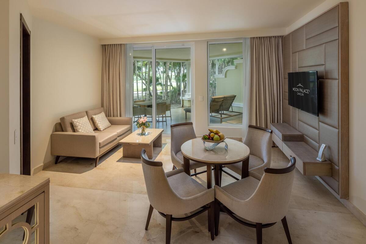 Uma sala de estar moderna com sofá, mesa de centro e mesa de jantar redonda com cadeiras. Uma televisão de tela plana está fixada na parede.