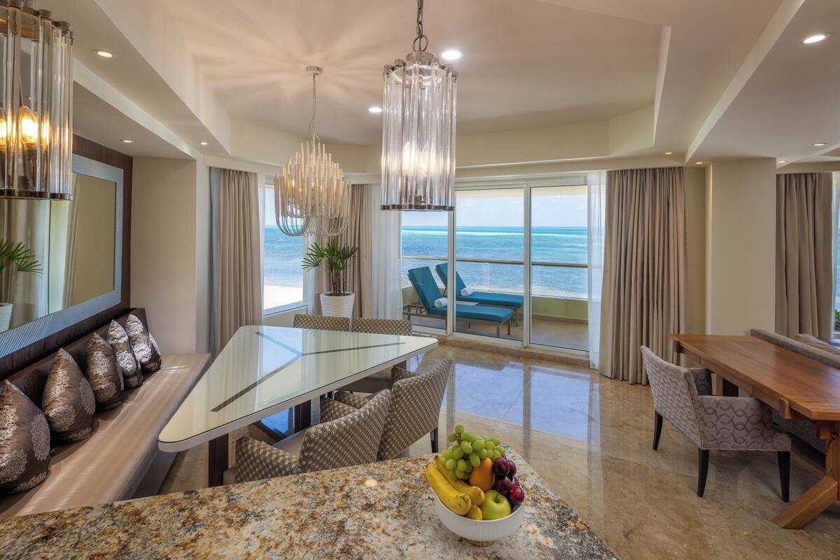 Quarto de hotel moderno com área de refeições, espaço de estar com vista para o oceano e varanda com vista para o mar.