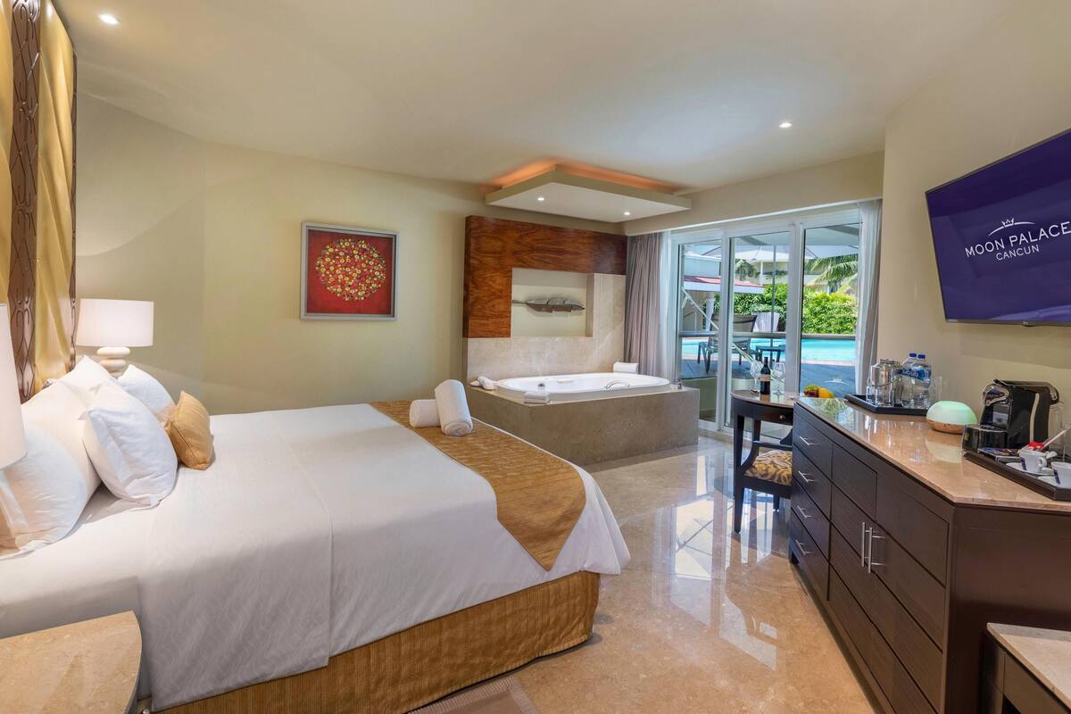 Quarto de hotel com cama, escrivaninha, televisão, banheiro com banheira e vista para a área da piscina.