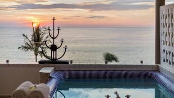Piscina com vista para o pôr do sol, um candelabro e toalhas sobre uma mesa.