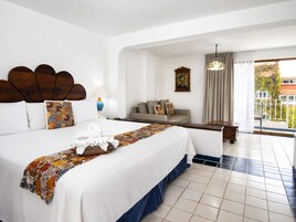 Quarto de hotel com cama, sofá, mesa de jantar e varanda com vista.