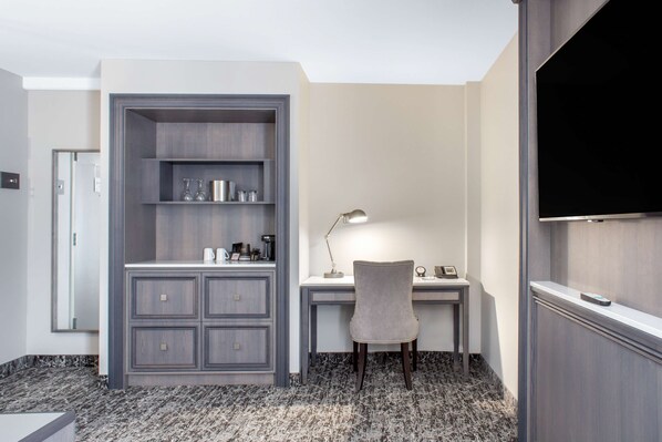 Quarto de hotel moderno com secretária embutida, uma cadeira, televisão e minibar.