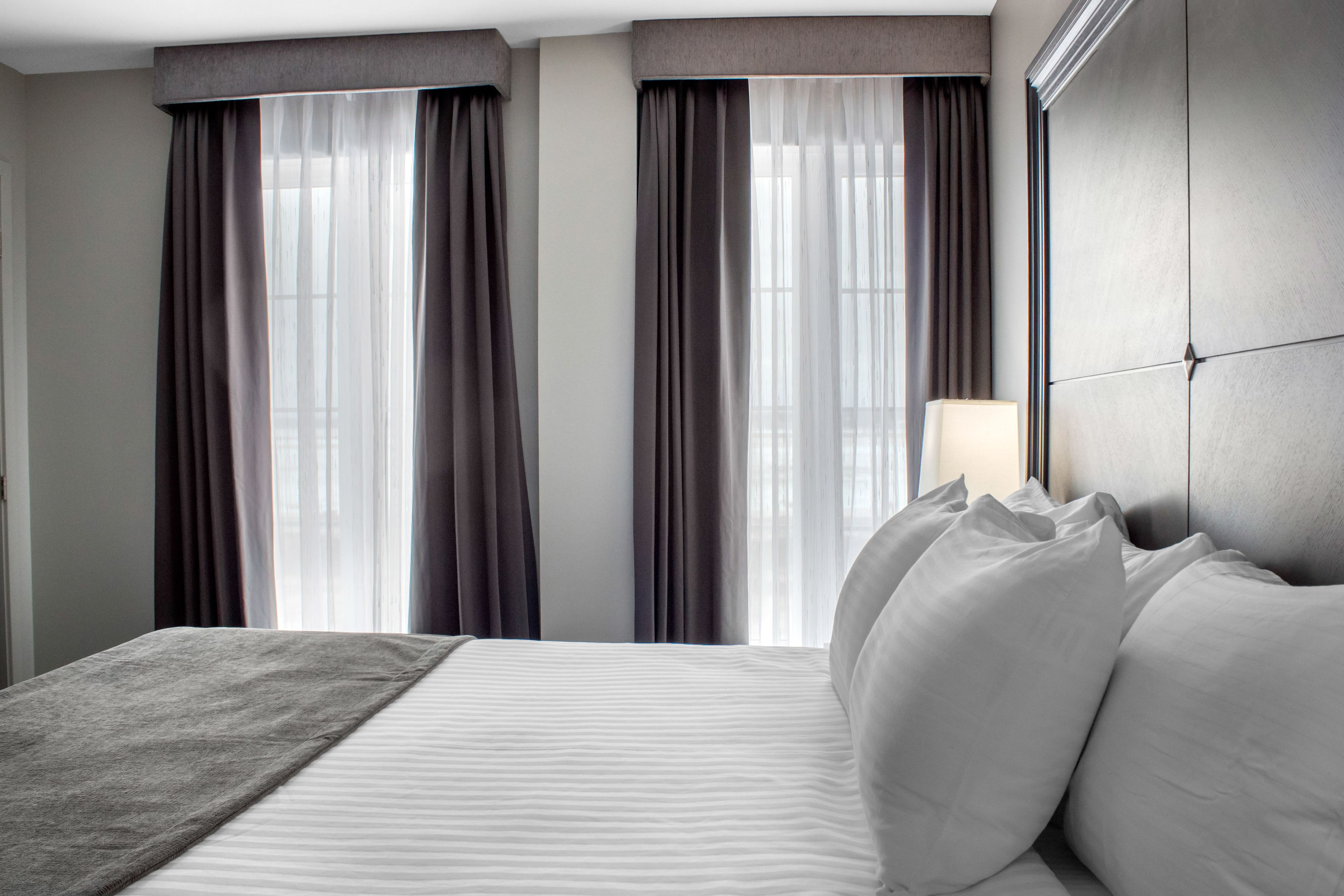 Quarto de hotel com uma cama, cortinas e uma mesa de cabeceira com abajur.
