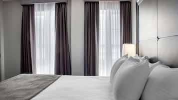 Quarto de hotel com uma cama, cortinas e uma mesa de cabeceira com abajur.