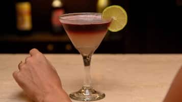 Um copo de martini com uma bebida em camadas e um toque de limão sobre uma superfície de mármore.