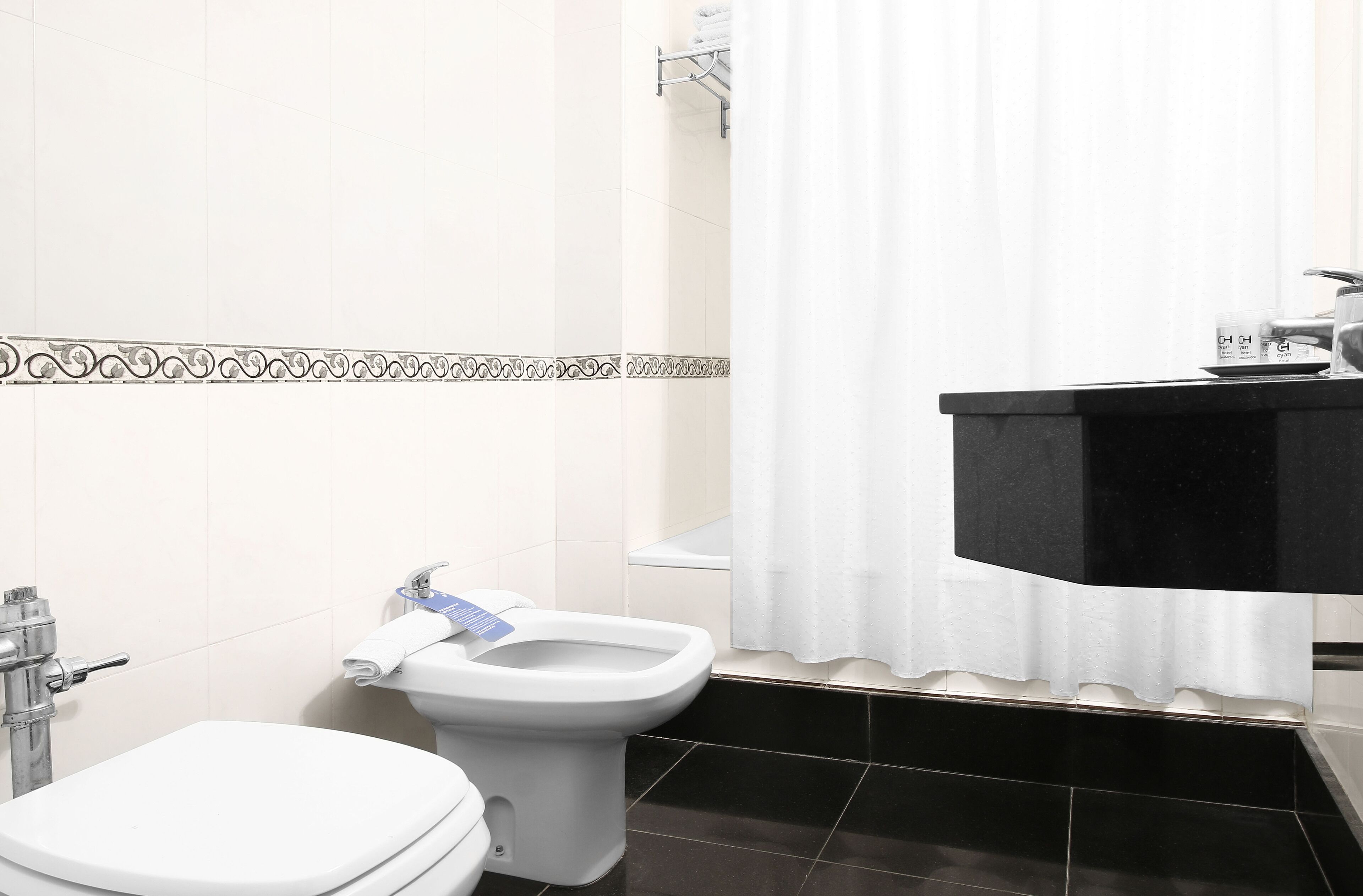 Casa de banho com sanita, bidé e lavatório com bancada preta.