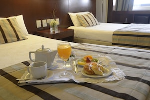 Bandeja de café da manhã bem arrumada com croissants, frutas e suco de laranja sobre a cama em um quarto de hotel.
