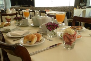 Disposição para o pequeno-almoço com croissants, fruta e sumo numa mesa.