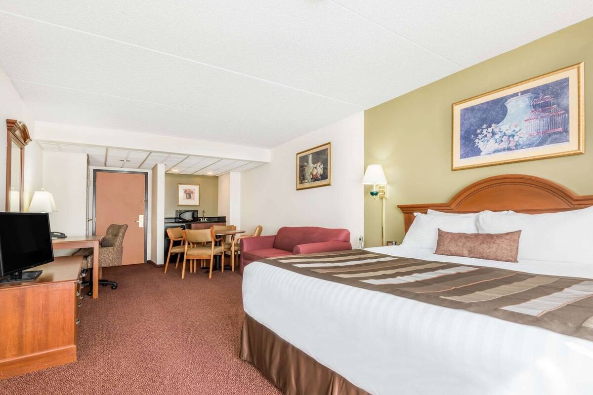 Quarto de hotel com uma cama, uma mesa com computador, uma cadeira, um sofá e um espaço para refeições.