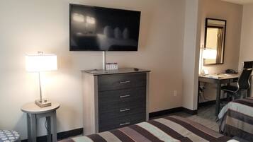 Quarto de hotel com cama, penteadeira, escrivaninha, cadeira, televisão e luminária.