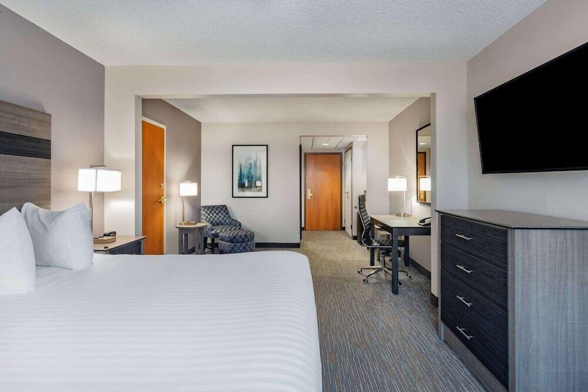 Quarto de hotel com cama, escrivaninha, cadeira e televisão.