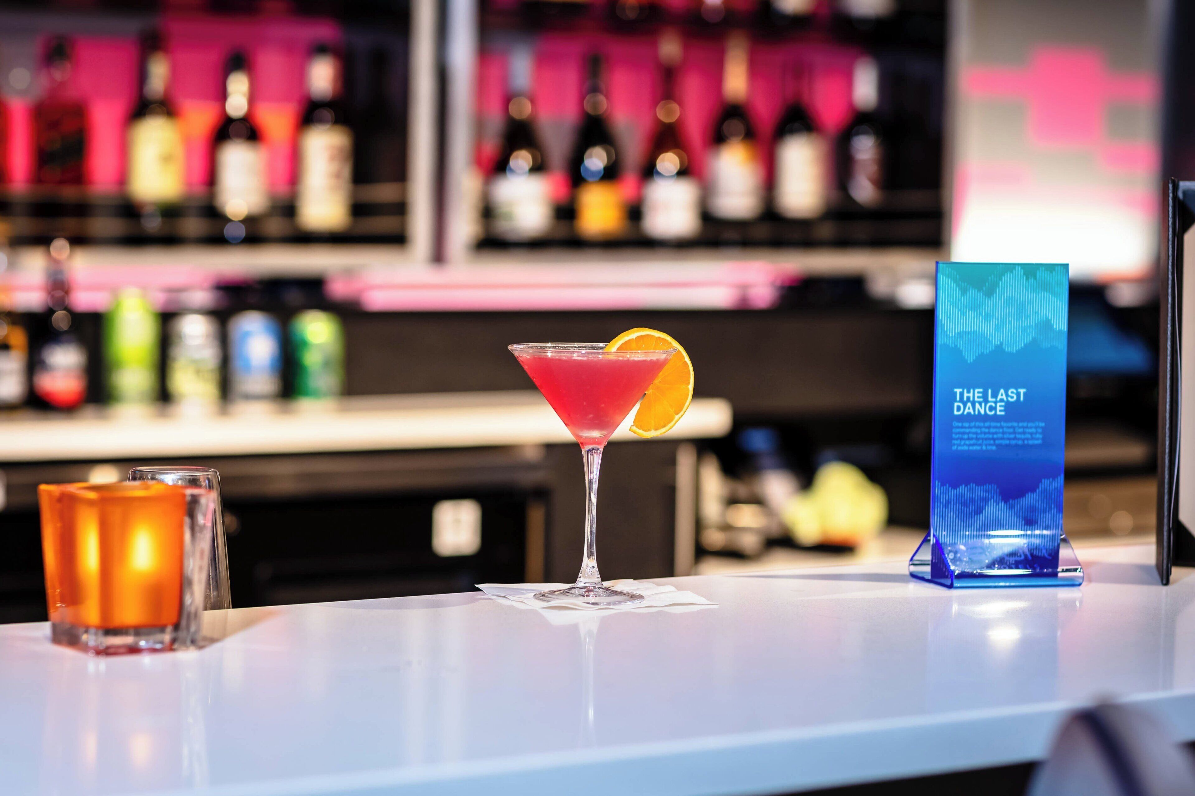 Uma área de bar com uma taça de martini e um coquetel, uma garrafa de licor, e um letreiro com o texto 'THE LAST DANCE'.
