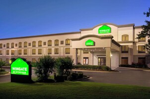 Hotel com um letreiro verde chamativo com a inscrição "Wingate by Wyndham" e um gramado bem cuidado na frente.