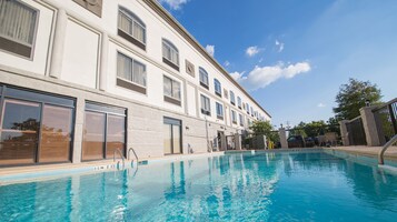Piscina com superfície de água azul cristalina, adjacente a um edifício com vários andares, grandes janelas e varanda.