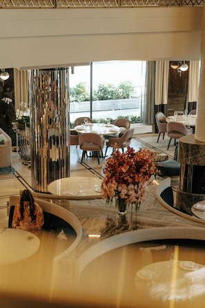 Uma área de jantar moderna com mesas redondas, cadeiras e um vaso decorativo com flores.