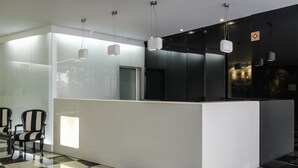 Uma área de recepção moderna com piso xadrez, um balcão de atendimento e duas cadeiras listradas em preto e branco.