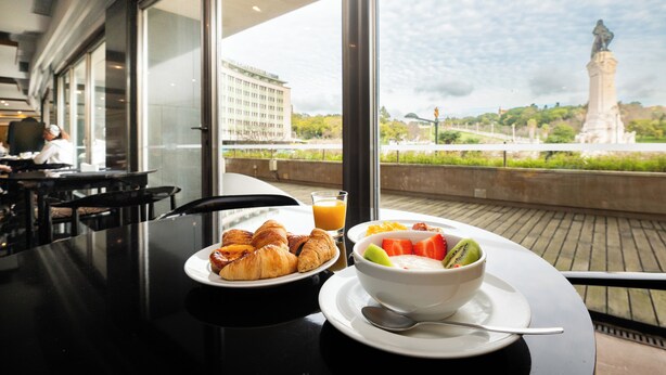 Uma mesa de café da manhã com croissants, uma tigela de frutas e iogurte, e um copo de suco de laranja.