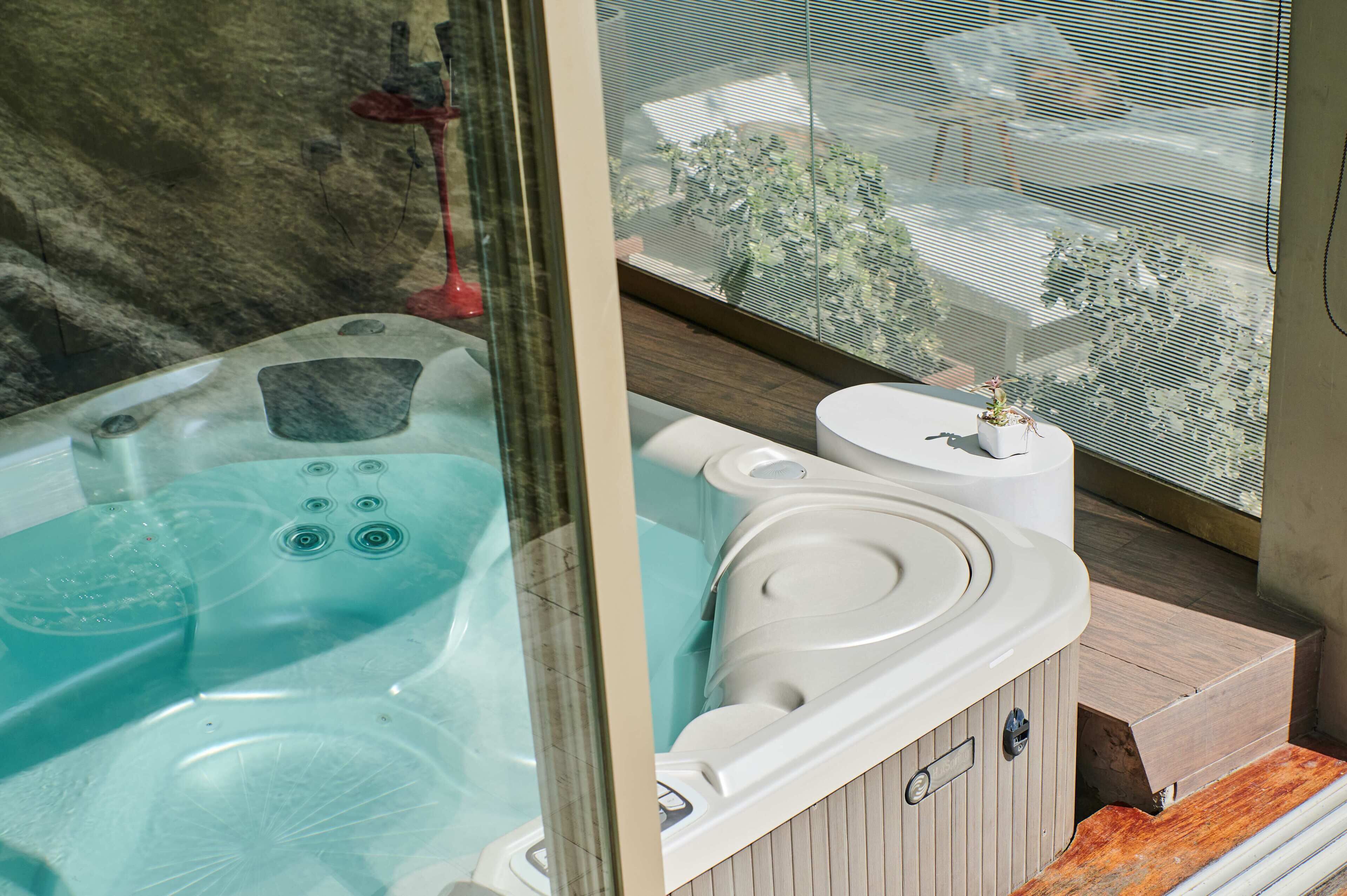 Uma área de spa com uma banheira de hidromassagem envidraçada, uma banheira menor independente e uma janela com vista para árvores.