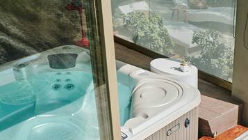 Uma área de spa com uma banheira de hidromassagem envidraçada, uma banheira menor independente e uma janela com vista para árvores.