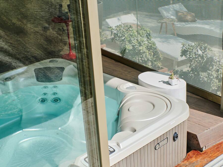 Uma área de spa com uma banheira de hidromassagem envidraçada, uma banheira menor independente e uma janela com vista para árvores.