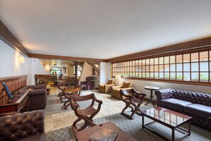 Ampla área de estar com sofás de couro, cadeiras de madeira e uma mesa de centro.