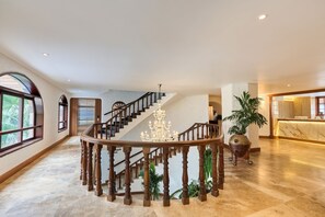 Um interior amplo com uma escadaria imponente, um lustre e uma área de recepção.