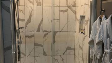 Uma casa de banho moderna com cabine de duche em vidro, azulejos de mármore e toalheiros com roupões.