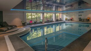 Piscina com deck revestido, cadeiras de descanso e vista para árvores através de grandes janelas.