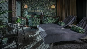 Quarto moderno com cama, duas poltronas, uma mesinha e um vaso de planta.